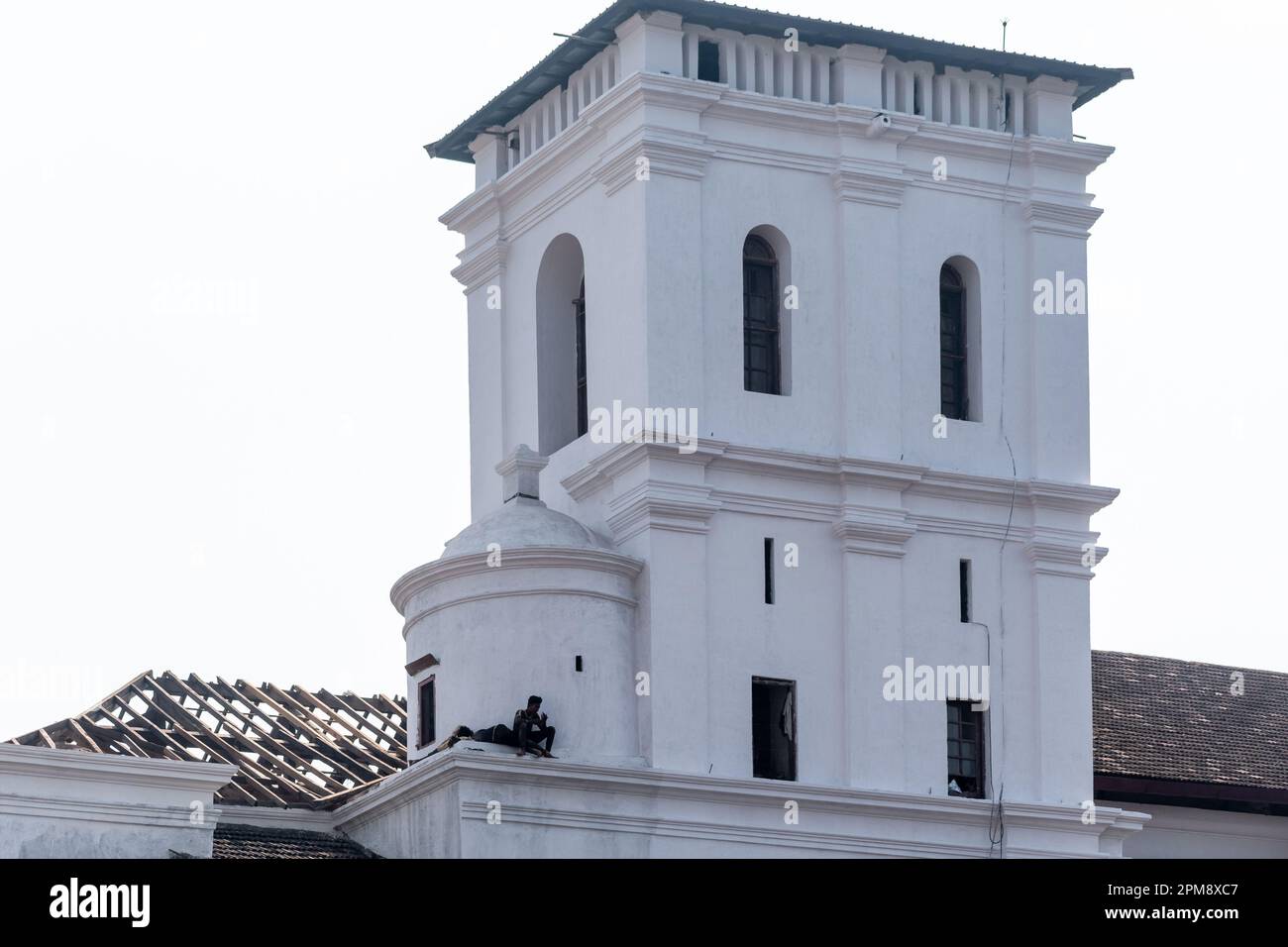Old Goa, India - January 2023: Two men sitting on a ledge on the roof ...