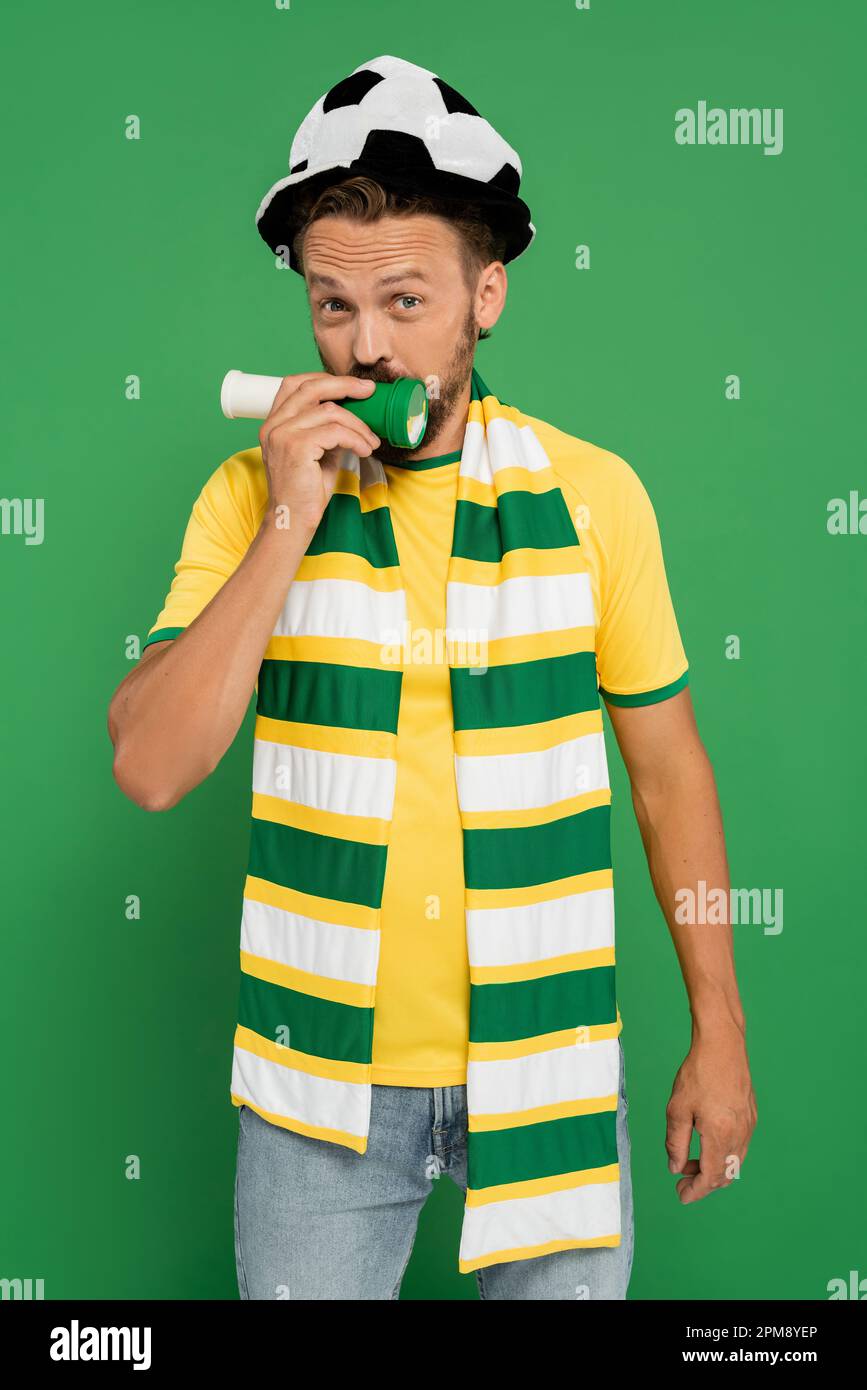 bearded man in sports hat blowing horn while cheering isolated on green ...