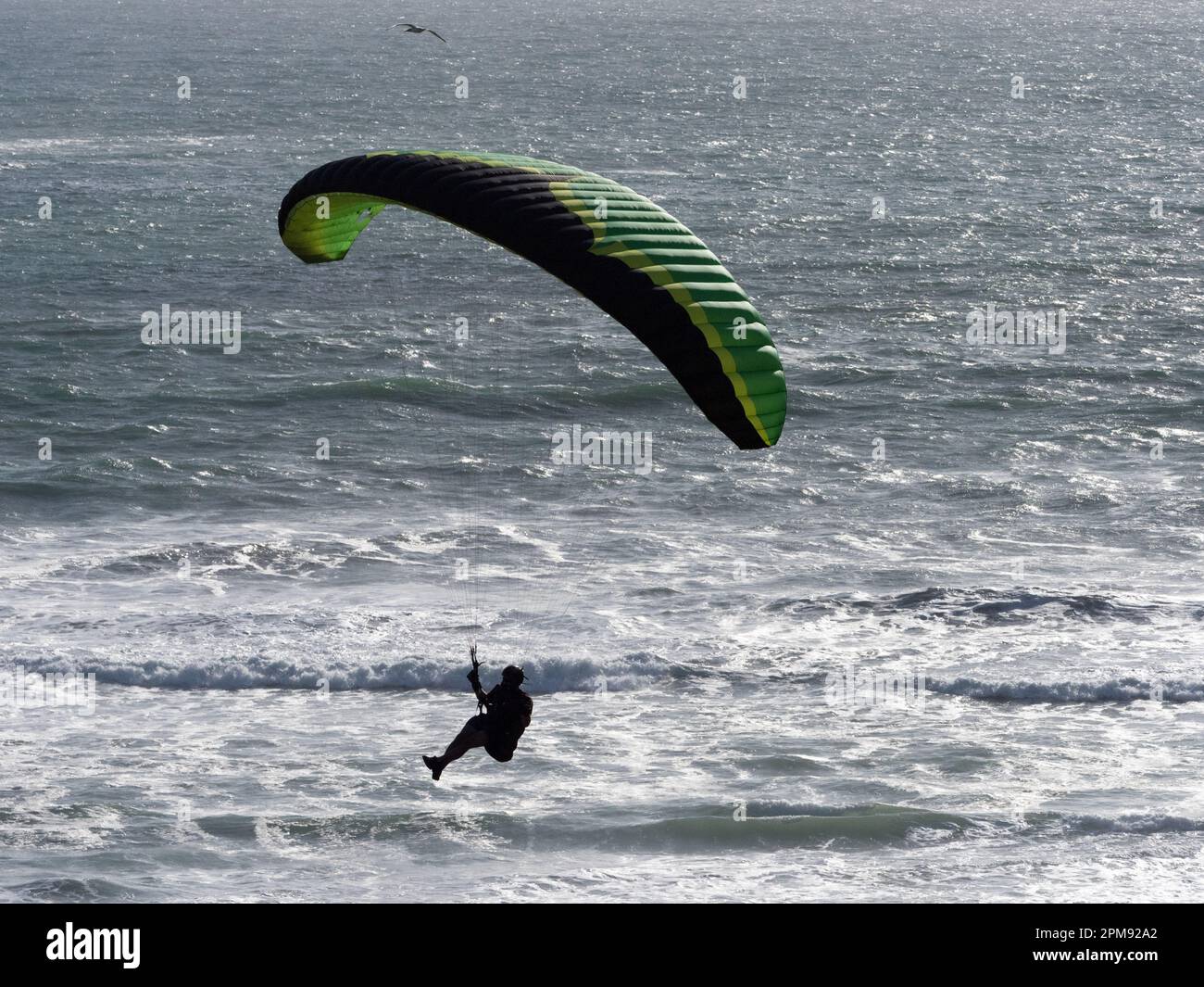 A paraglider flies above an ocean with waves.Backlit silhouette Stock ...