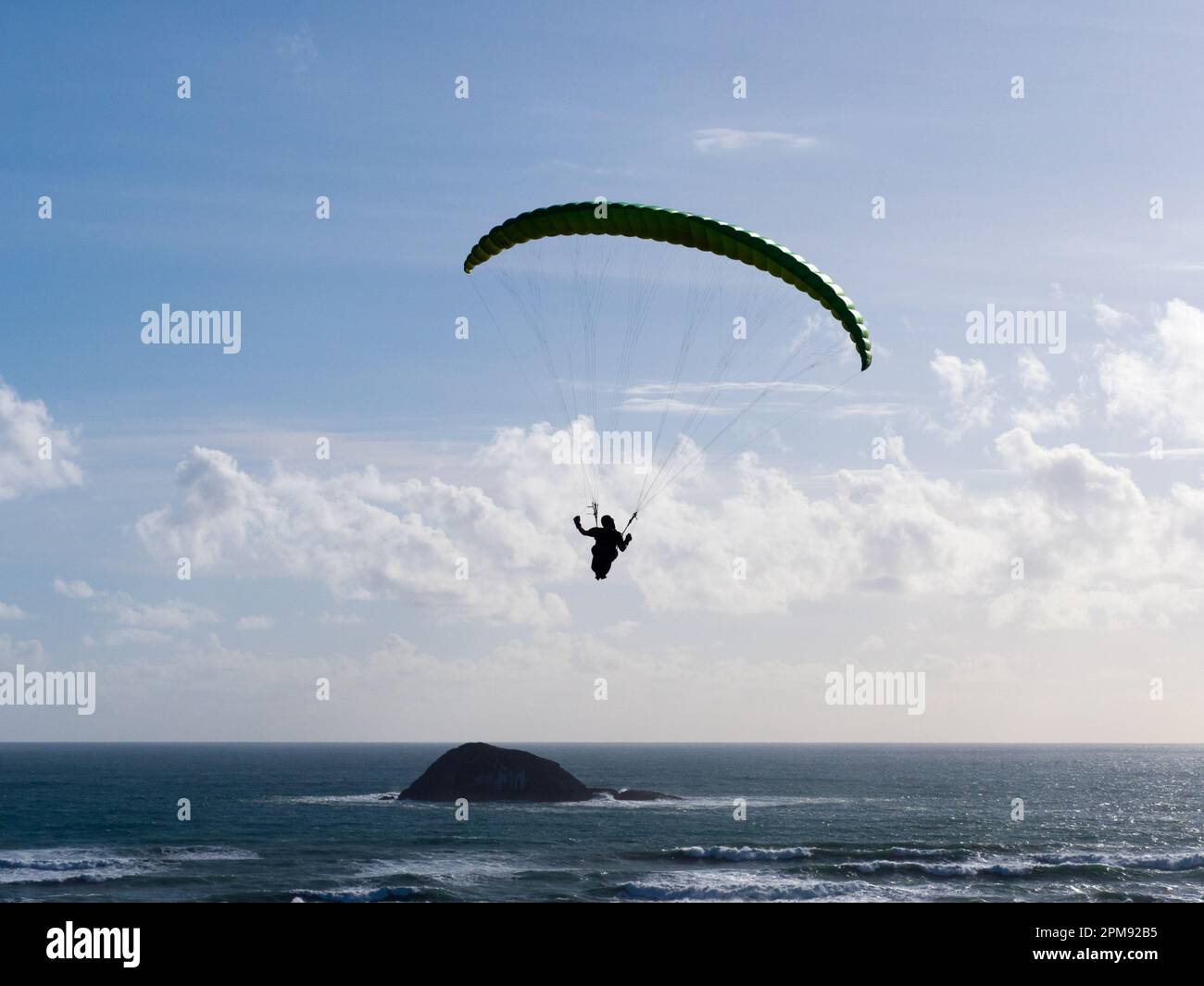 A paraglider flies over an ocean scene with an island.Backlit ...