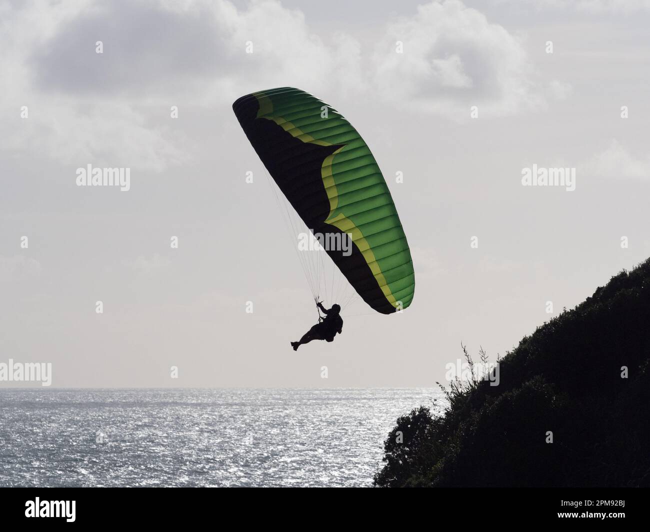 A paraglider flies over an ocean scene with an outcrop of land to his ...