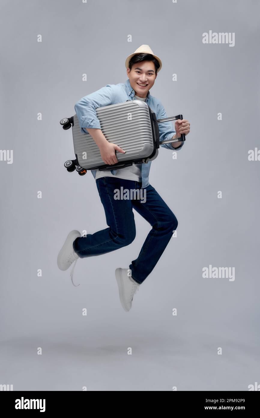 Smiling young handsome Asian tourist man with baggage jumping in mid ...