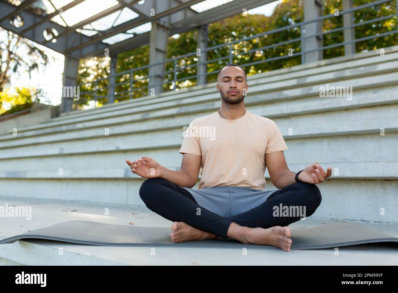 Young african american man doing yoga in stadium, urban. Sitting on a ...