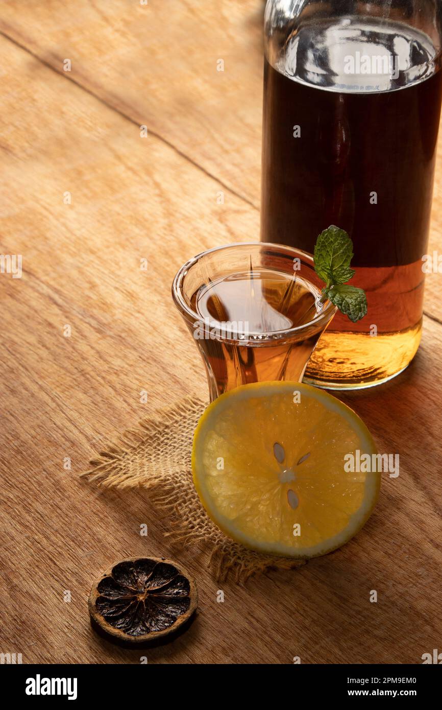 A vertical shot of a small shot glass with a lemon slice near a bottle ...