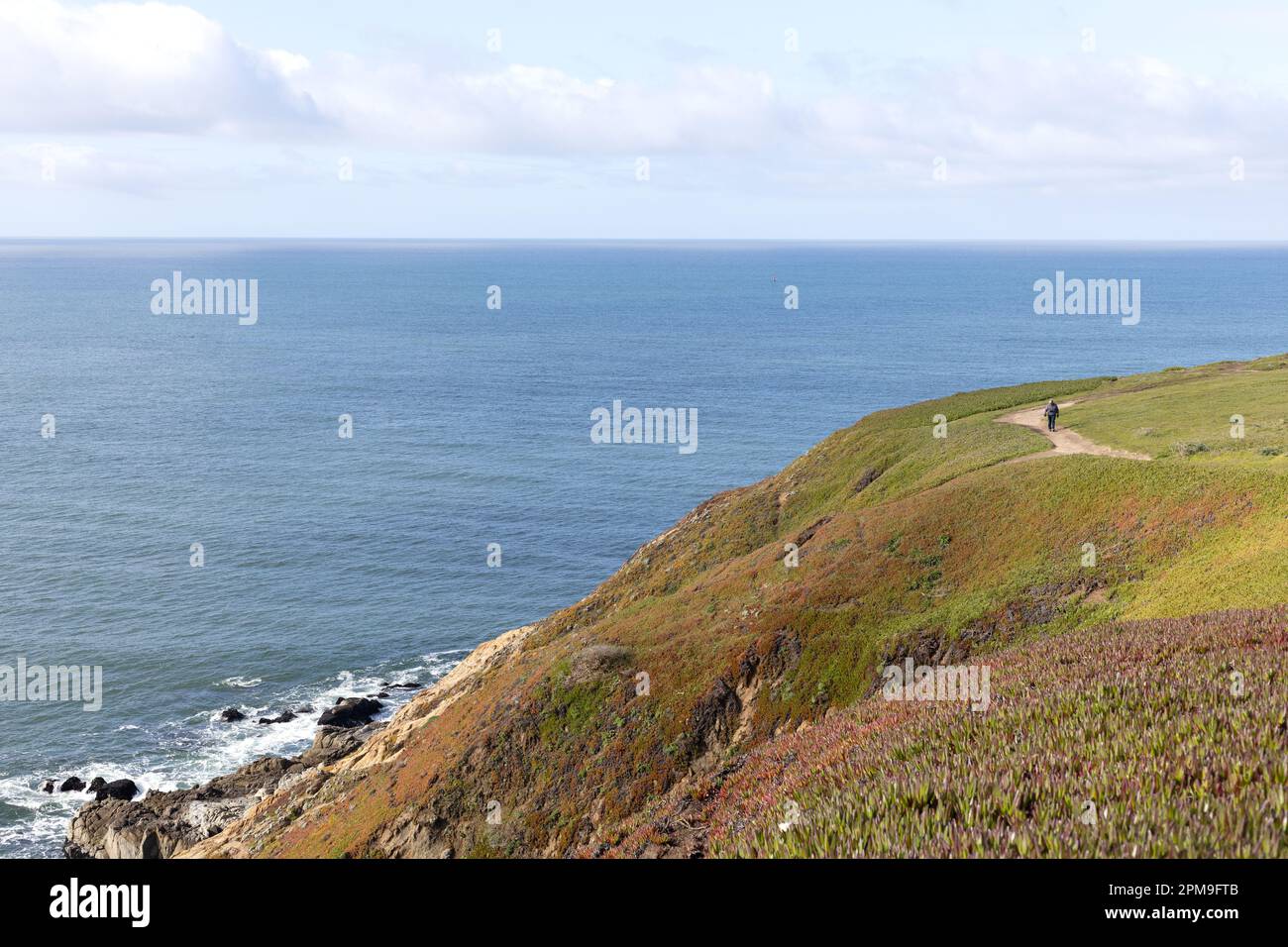 A person walking in the distance on a cliffside trail on a spring day ...
