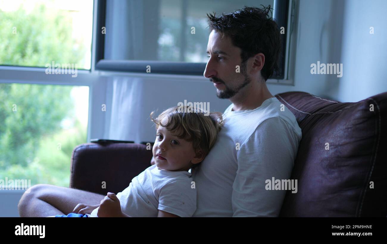 Son sitting on father lap at home couch indoors. Authentic real life ...