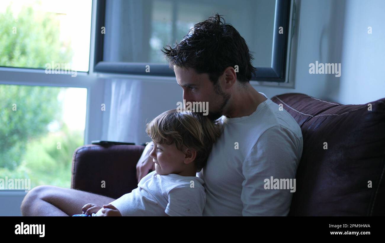 Son sitting on father lap at home couch indoors. Authentic real life ...