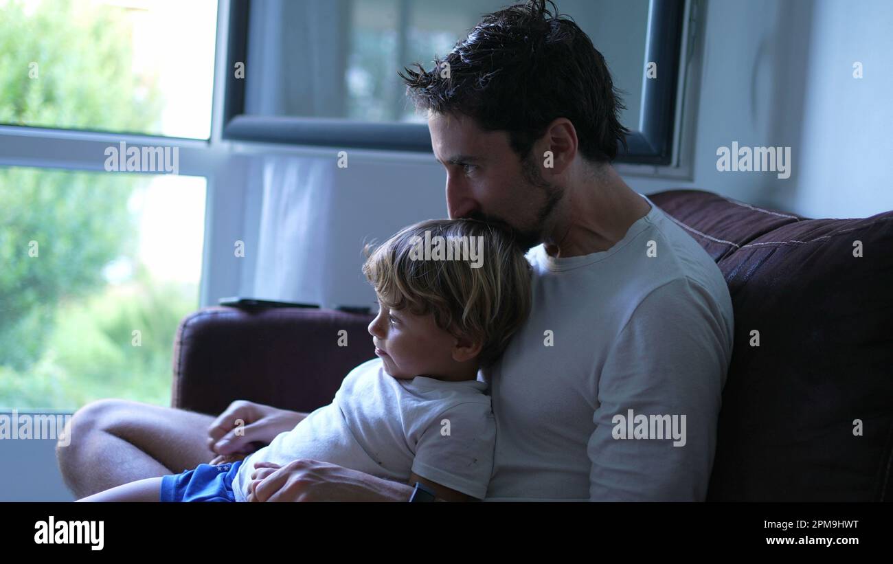 Son sitting on father lap at home couch indoors. Authentic real life ...