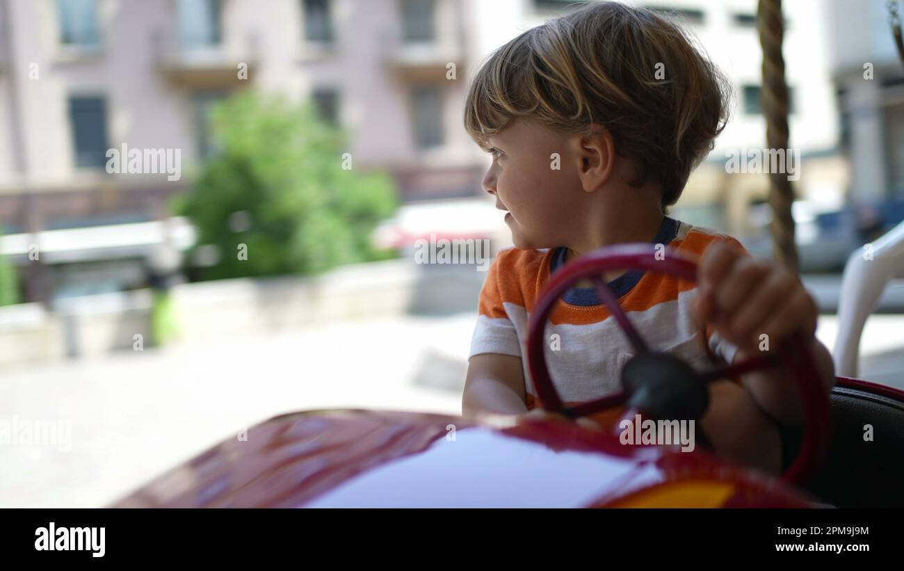 One happy small boy holding steering wheel inside a carousel car during ...