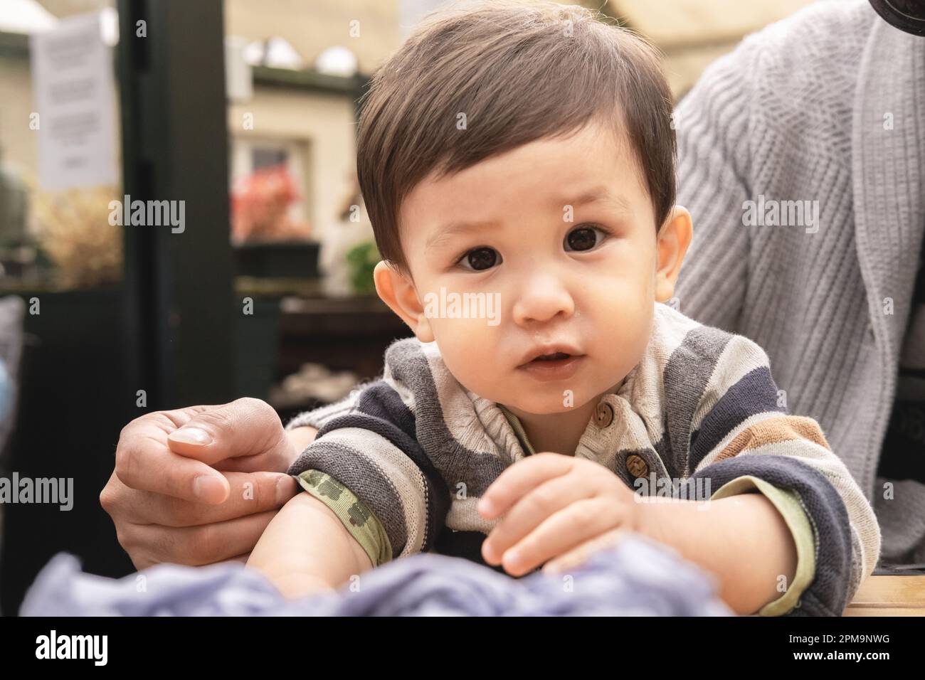 A male infant looking at camera staring with big brown eyes sitting on ...