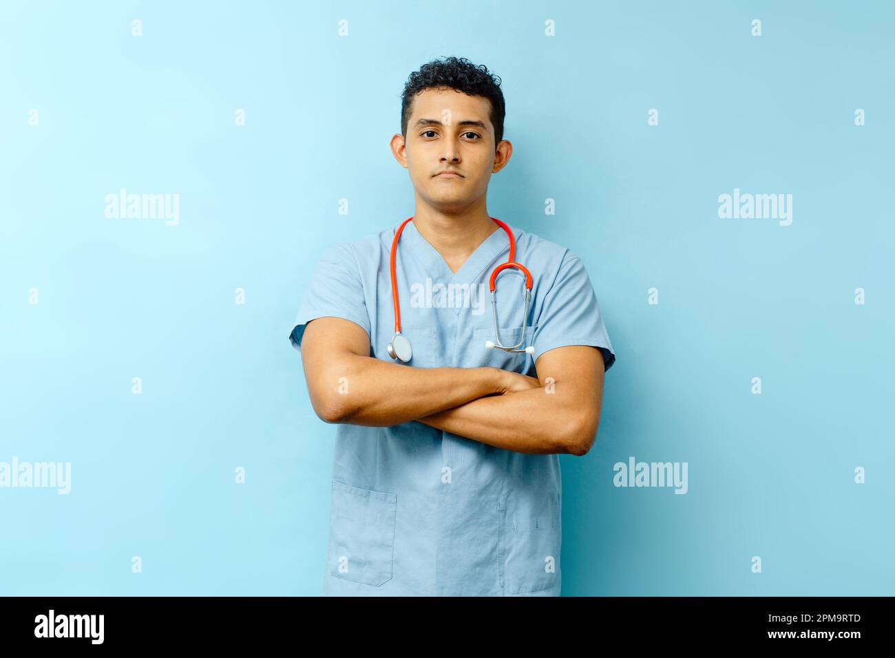 A male doctor stands confidently against a bright blue background with ...