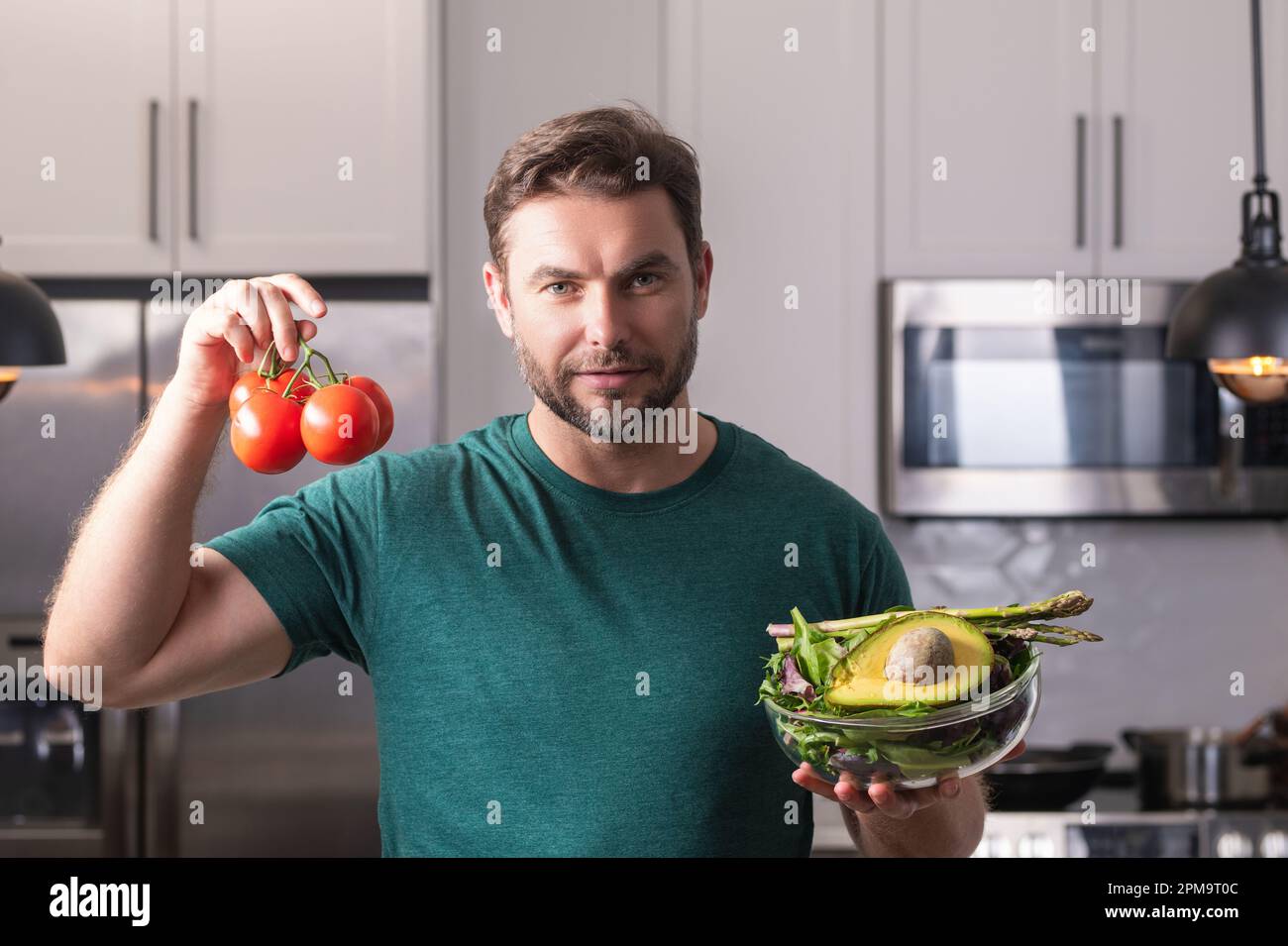 Man with a plate of vegetable salad in the kitchen. Man cooking vegan ...