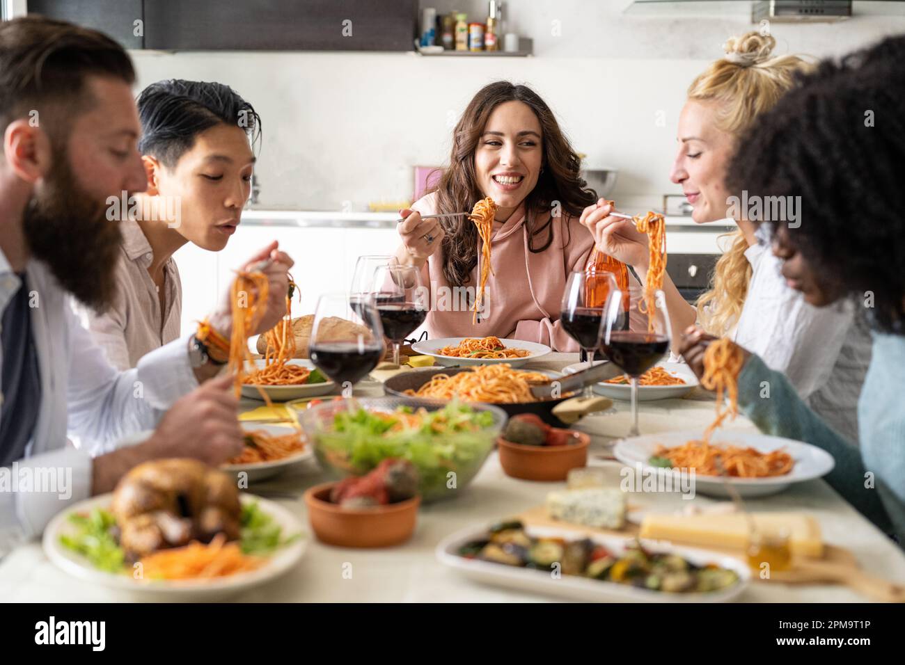 Lunch with friends, smiling young woman among people eating spaghetti ...