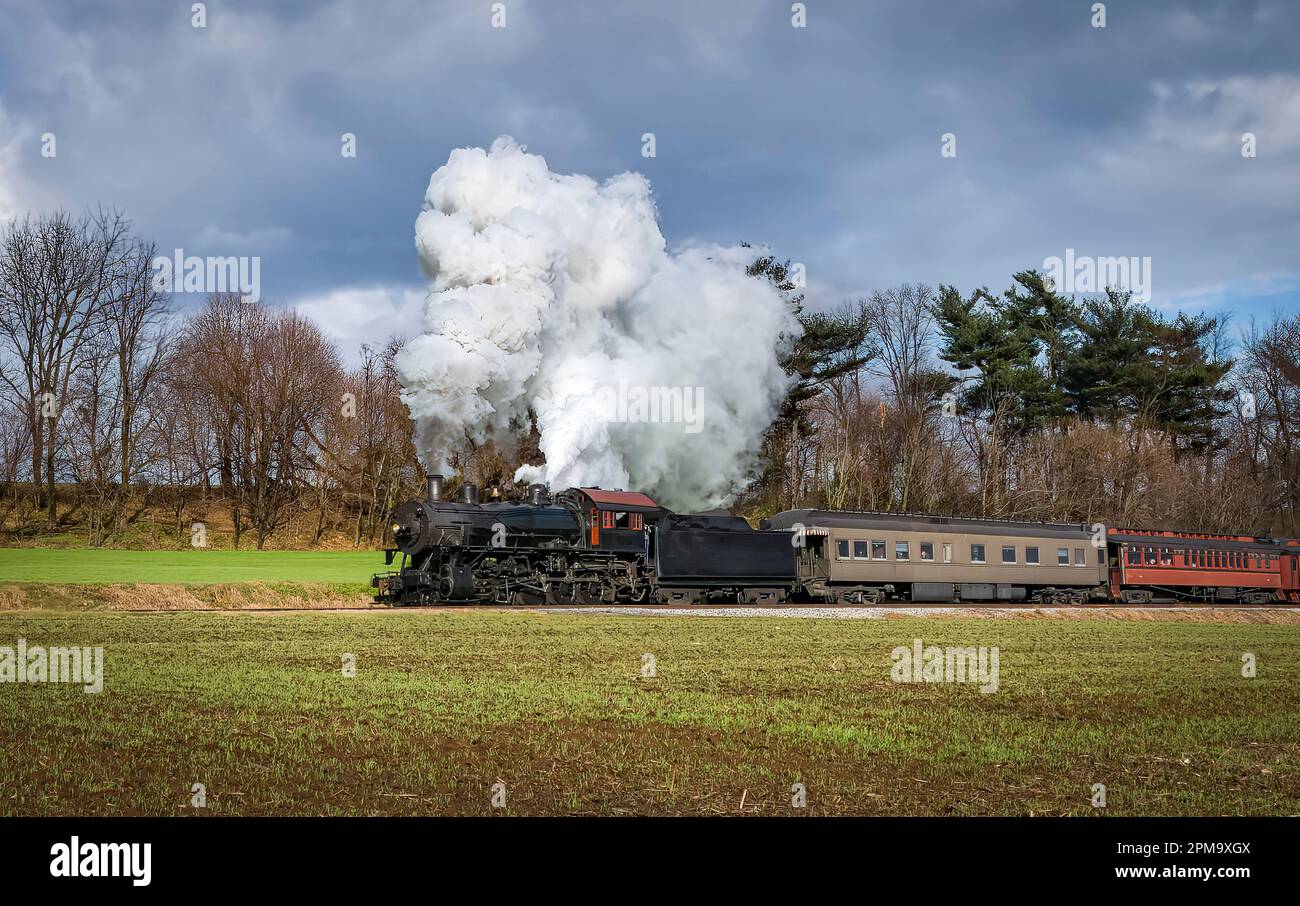A vintage steam locomotive engine is pictured traveling through a lush ...