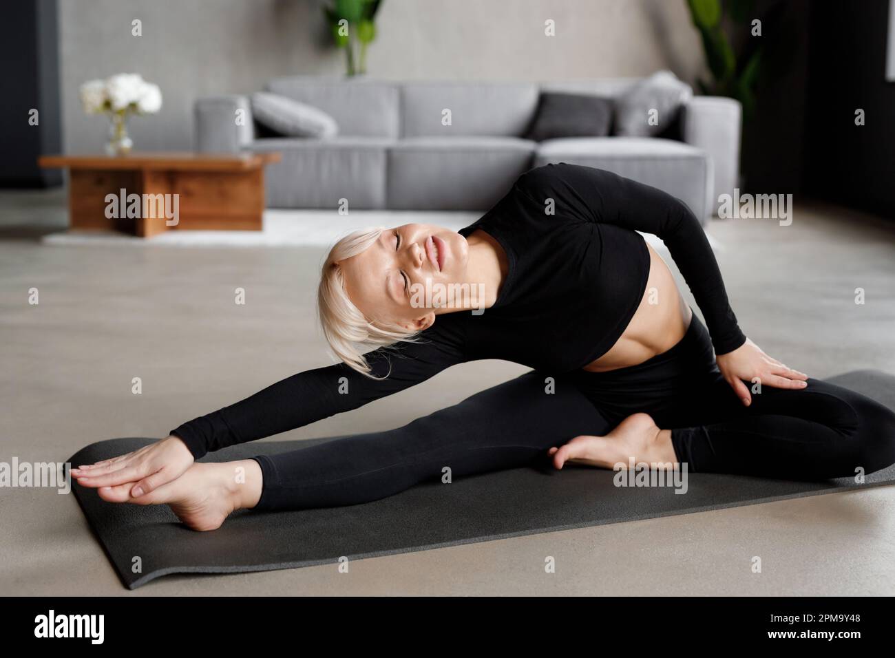 A young slim woman has done splits, and is stretching herself with her ...