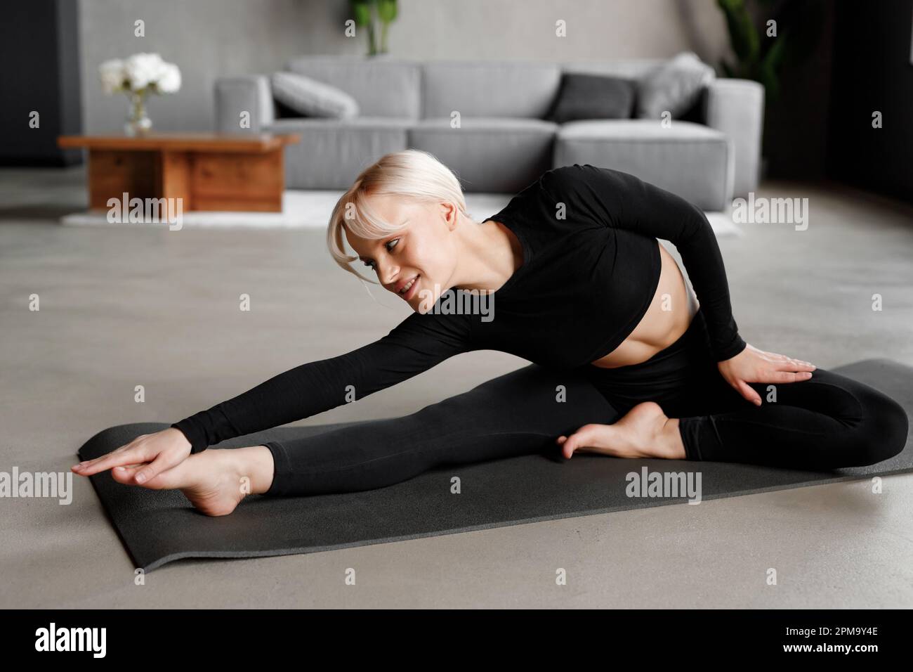 A young slim woman has done splits, and is stretching herself with her ...