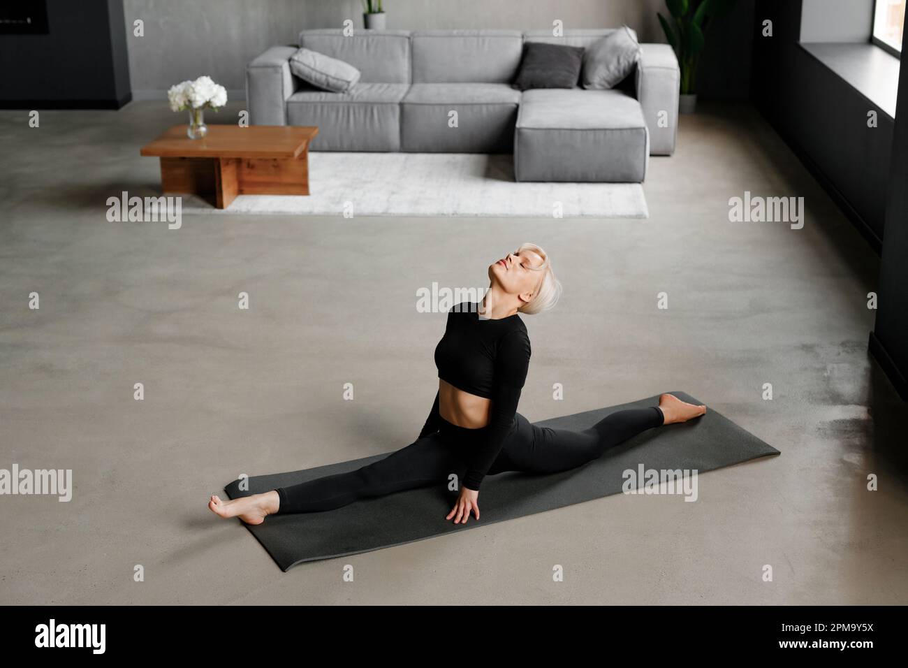 A young slender woman does splits to stretch her legs. Joyful talented ...