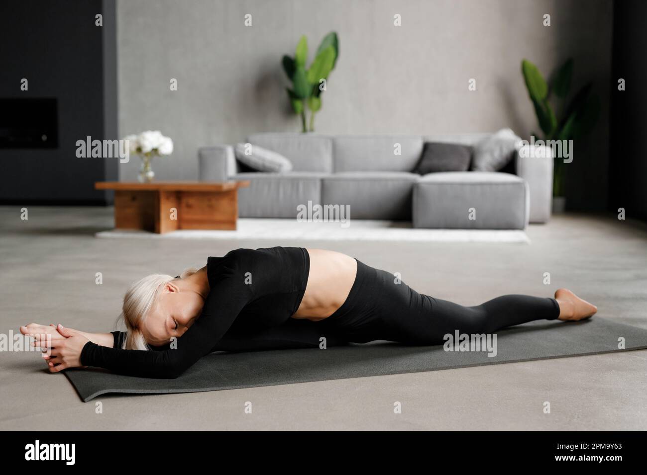 A young slender woman does splits to stretch her legs. Joyful talented ...