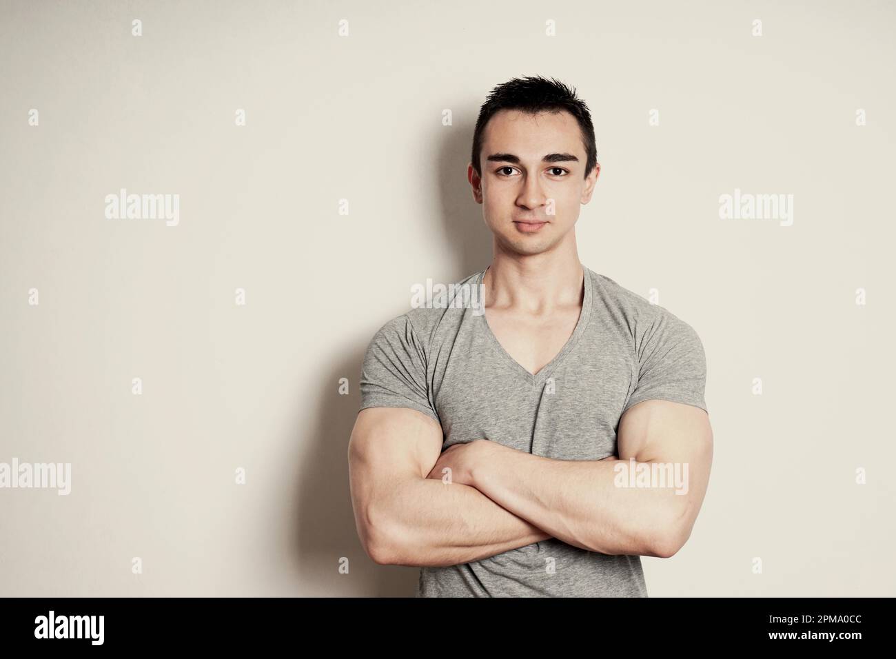 muscular young man with arms crossed standing against wall with copy space. vintage filter ...