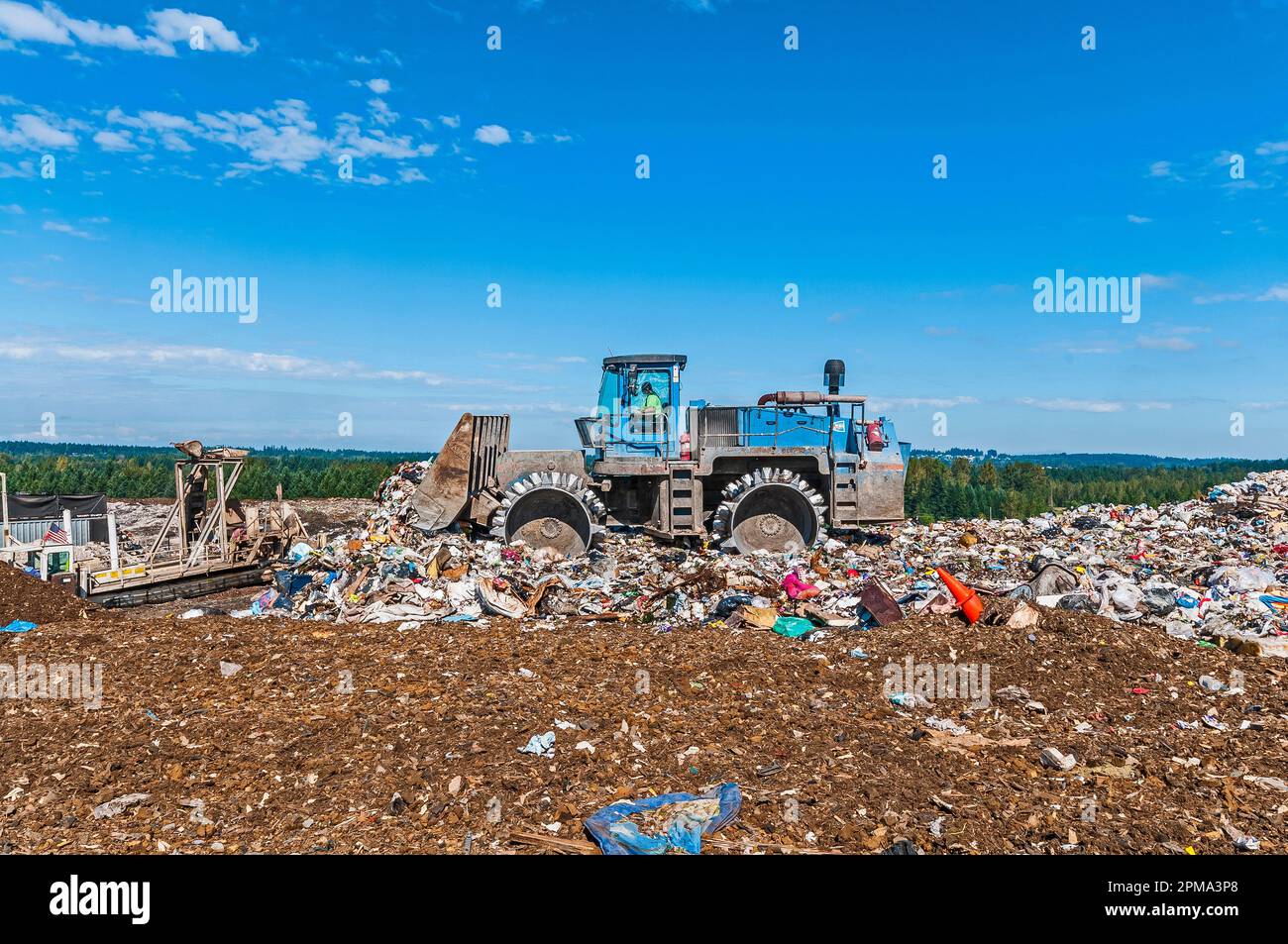 A soil compactor moving around and manipulating trash in the dirt on a ...