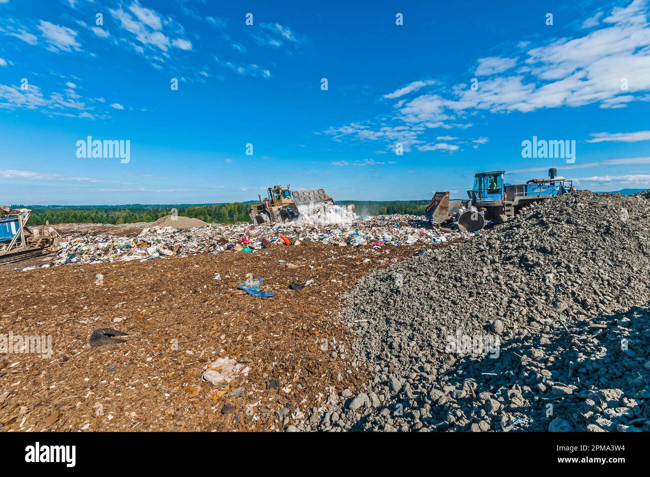Soil compactors moving around and manipulating trash in the dirt on a ...