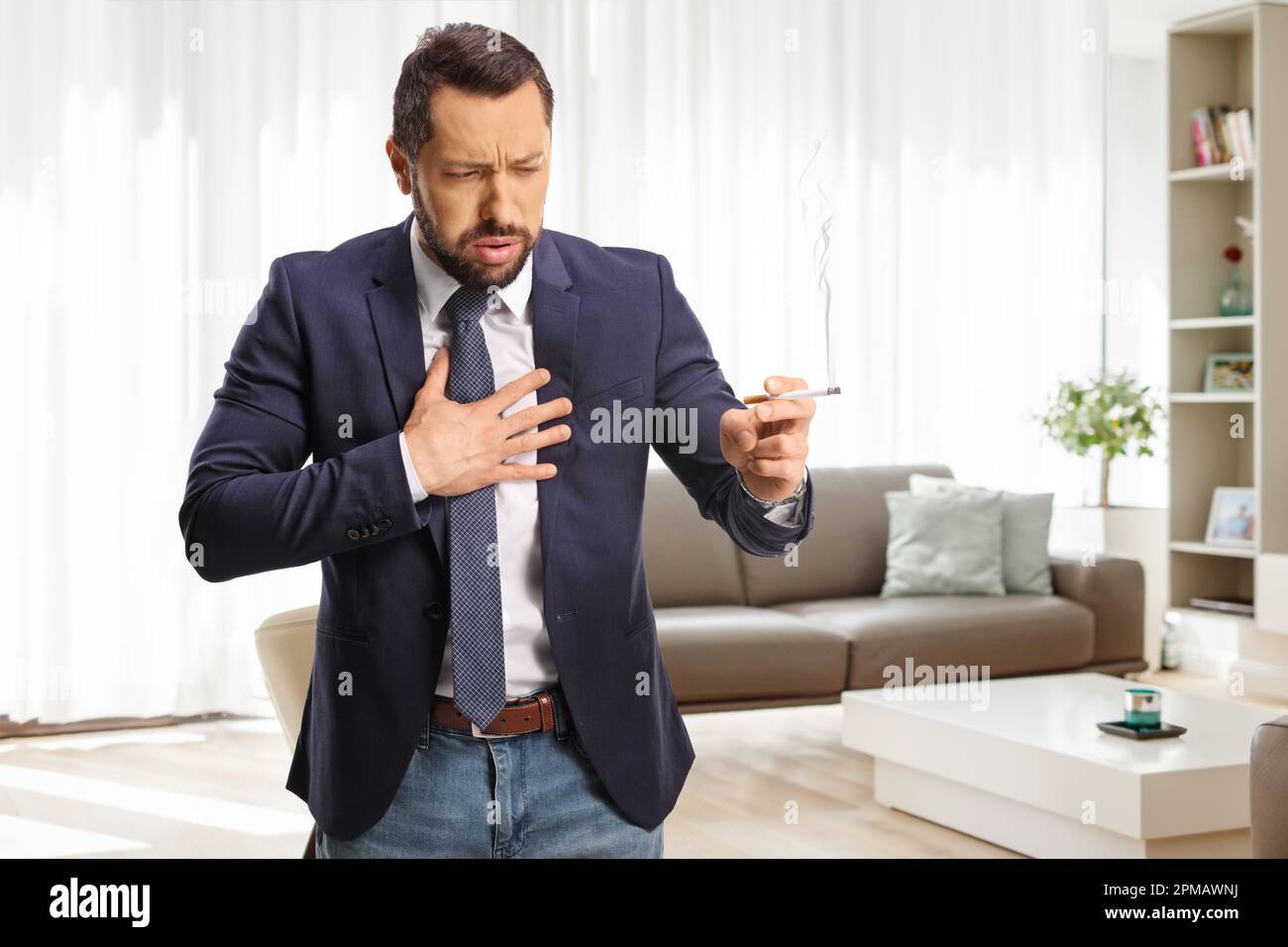 Man coughing and holding a cigarette indoors at home Stock Photo - Alamy