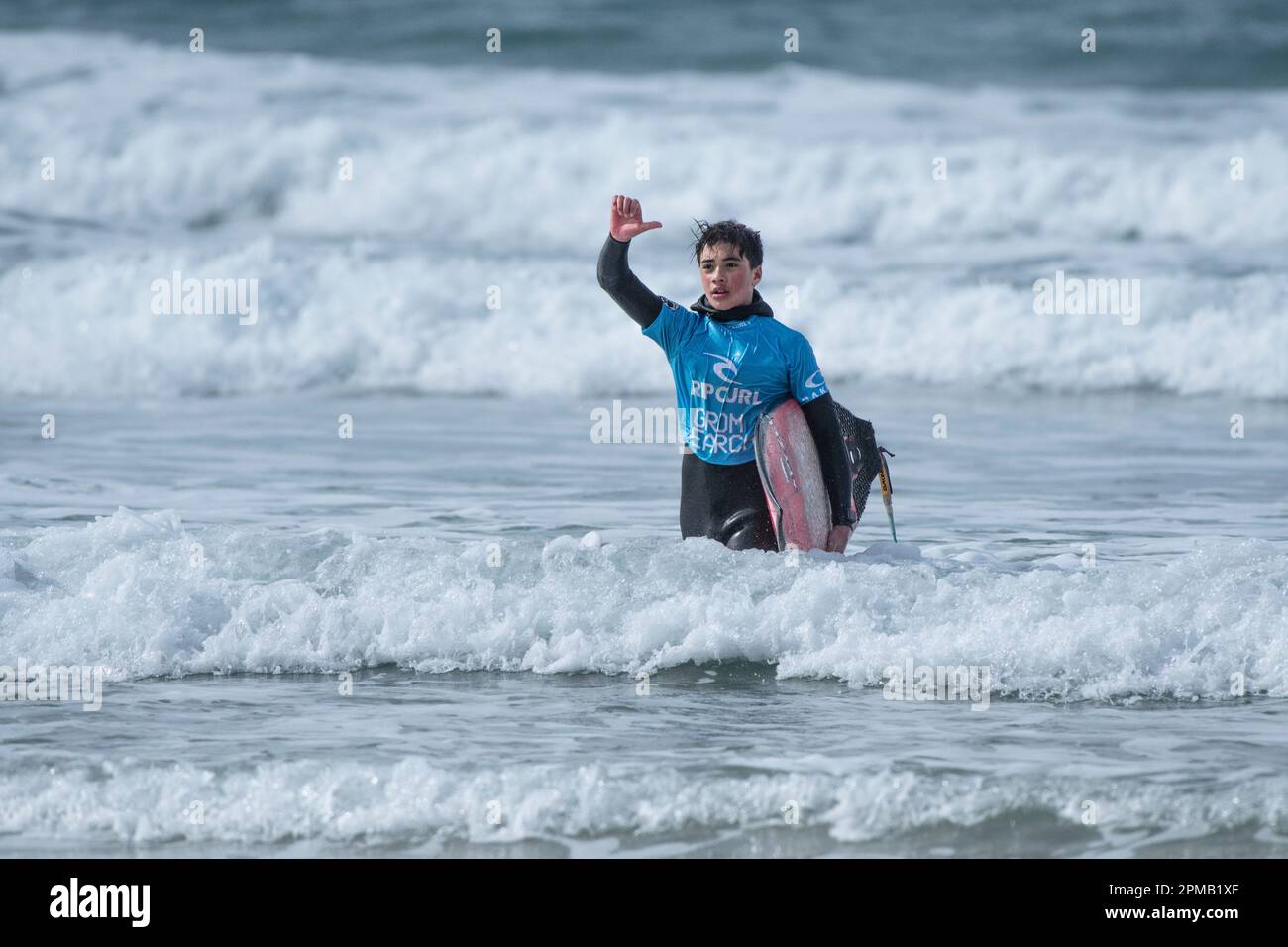 A young male surfer carrying his surfboard and waving and walking out ...