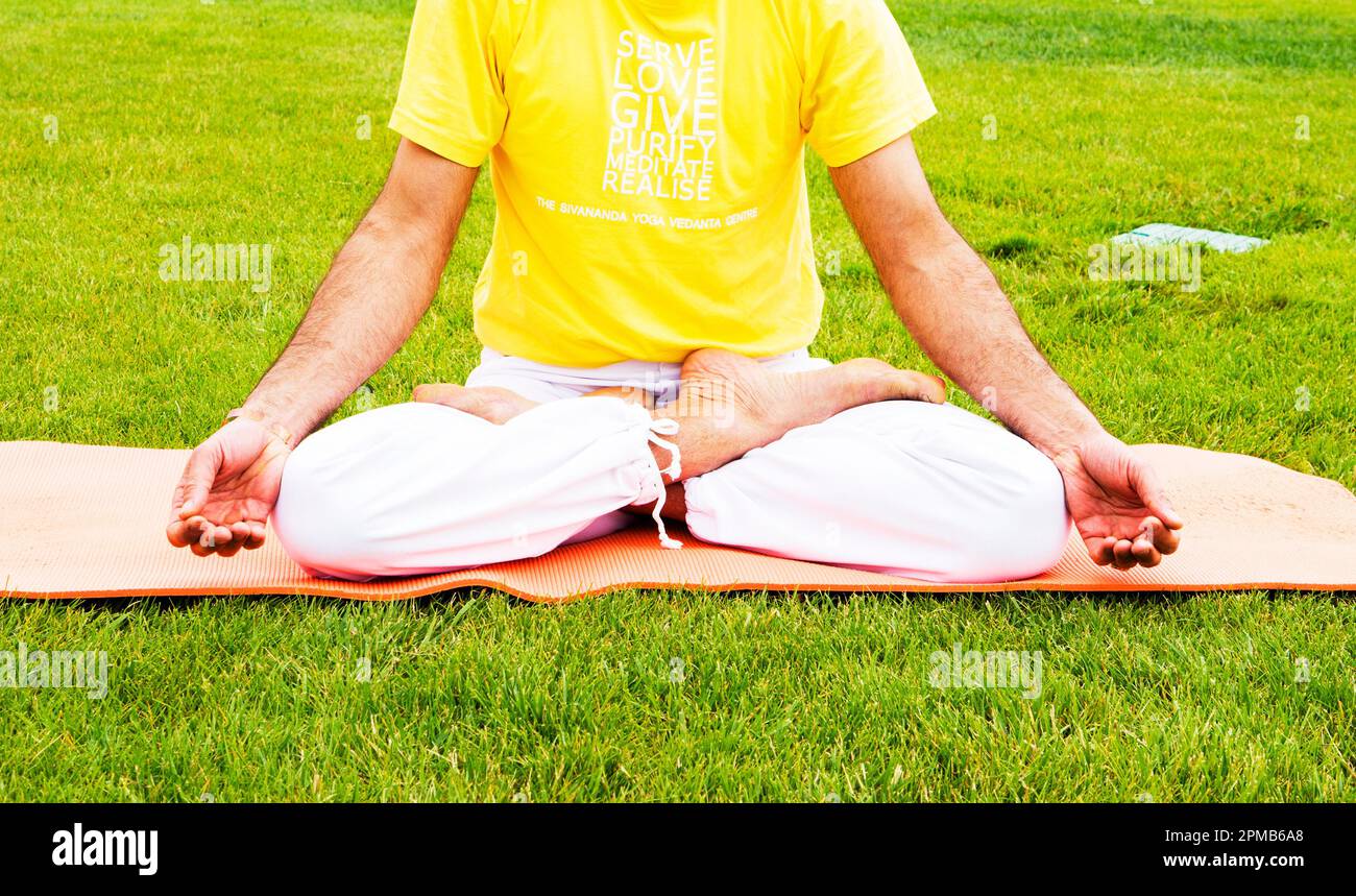 Young man sitting in yoga pose at green grass in the meadow and ...