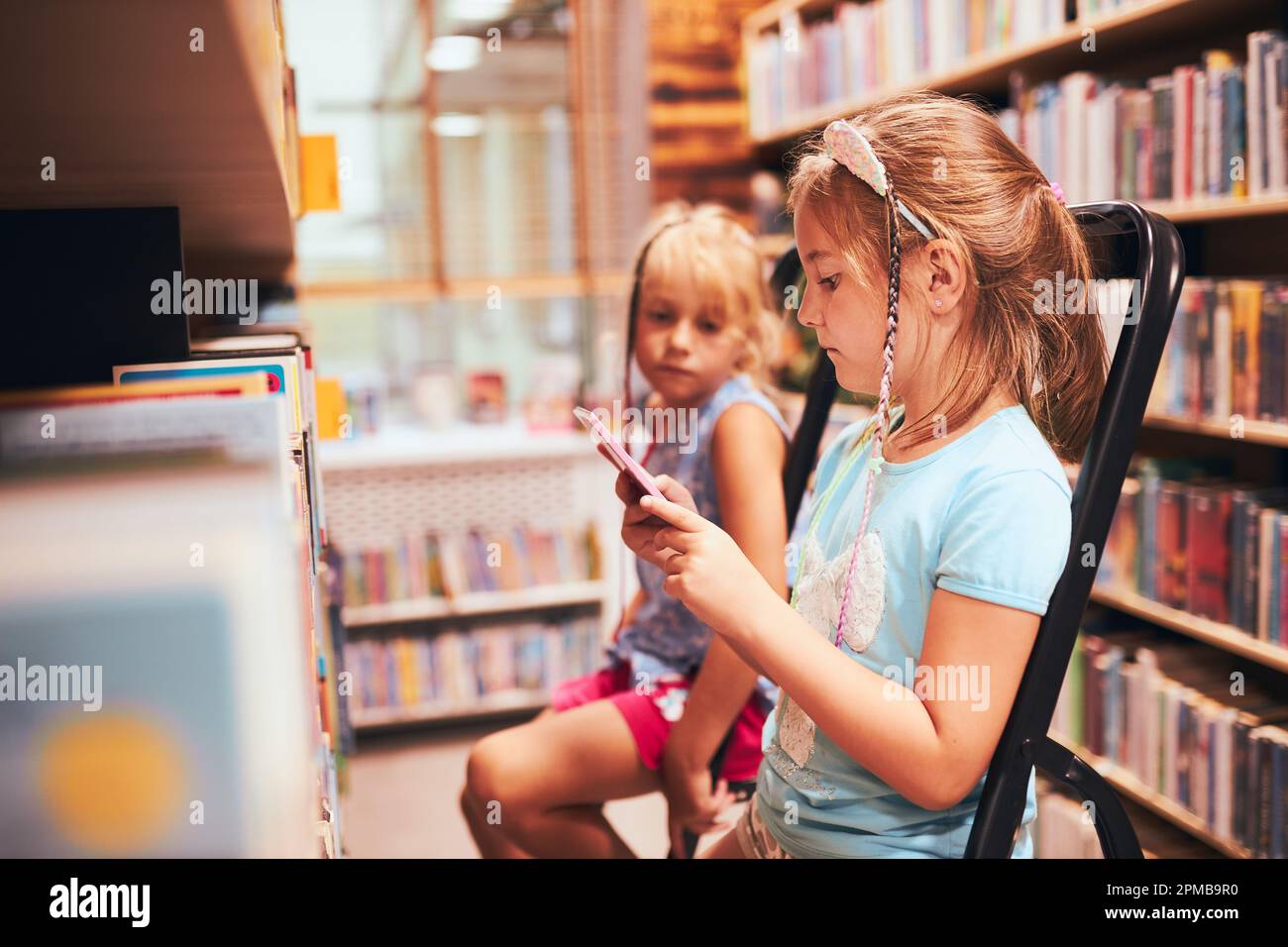 Schoolgirls looking for books in school library. Students choosing set ...