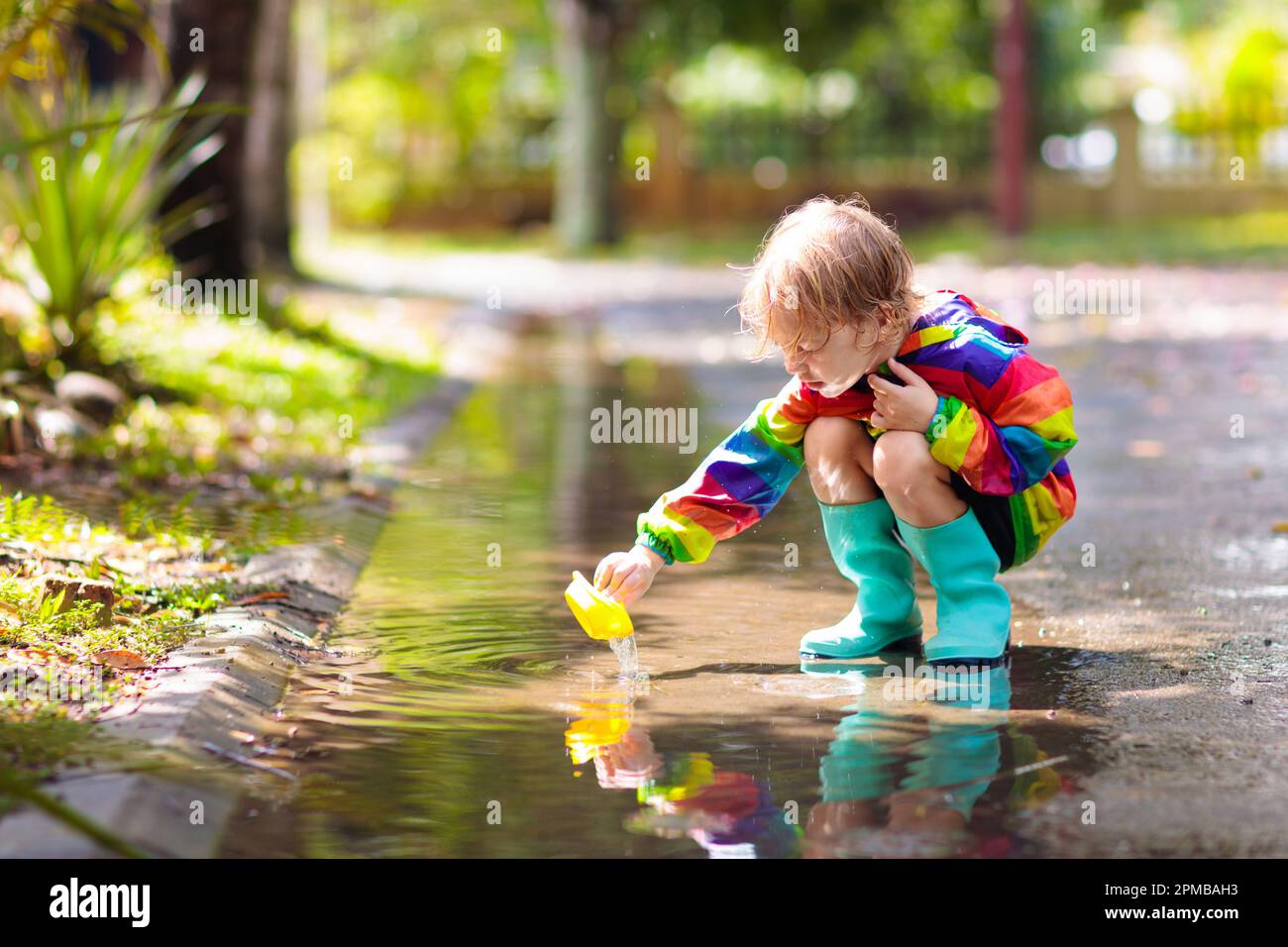 Kid playing in the rain in autumn park. Child jumping in muddy puddle ...