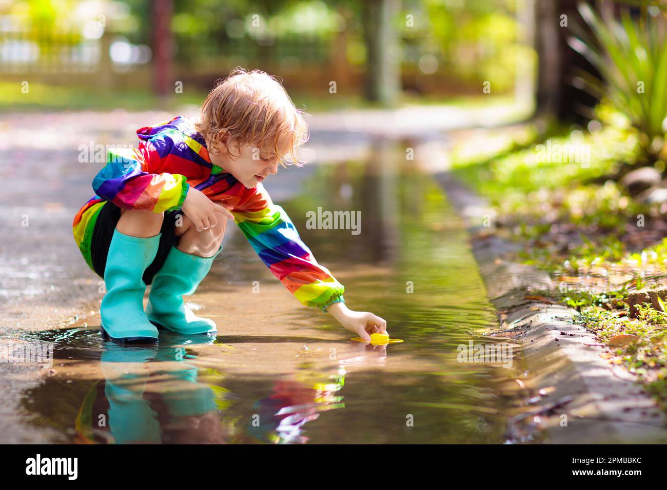 Kid playing in the rain in autumn park. Child jumping in muddy puddle ...