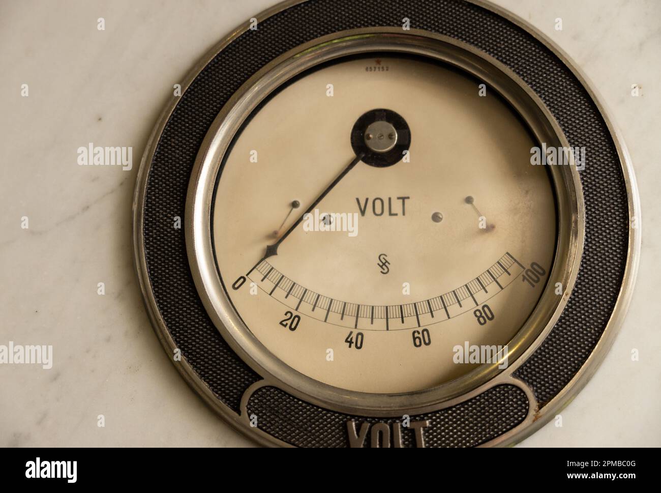 An antique non-functioning voltmeter in a round frame hangs on the wall ...