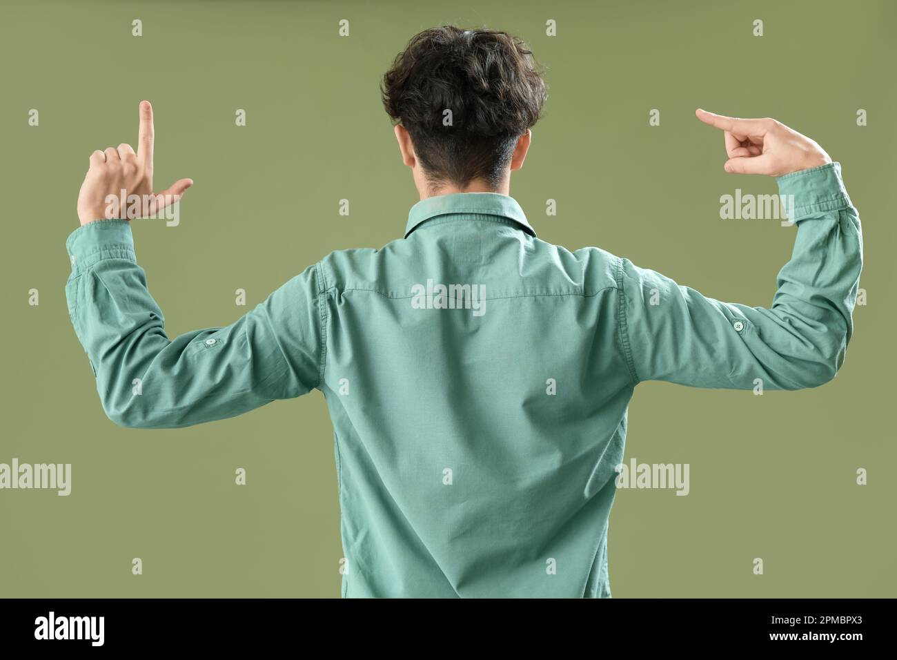 Young man showing loser gesture on green background, back view Stock ...