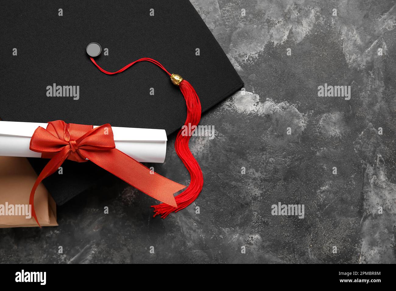 Diploma with red ribbon, graduation hat and book on dark grey table ...