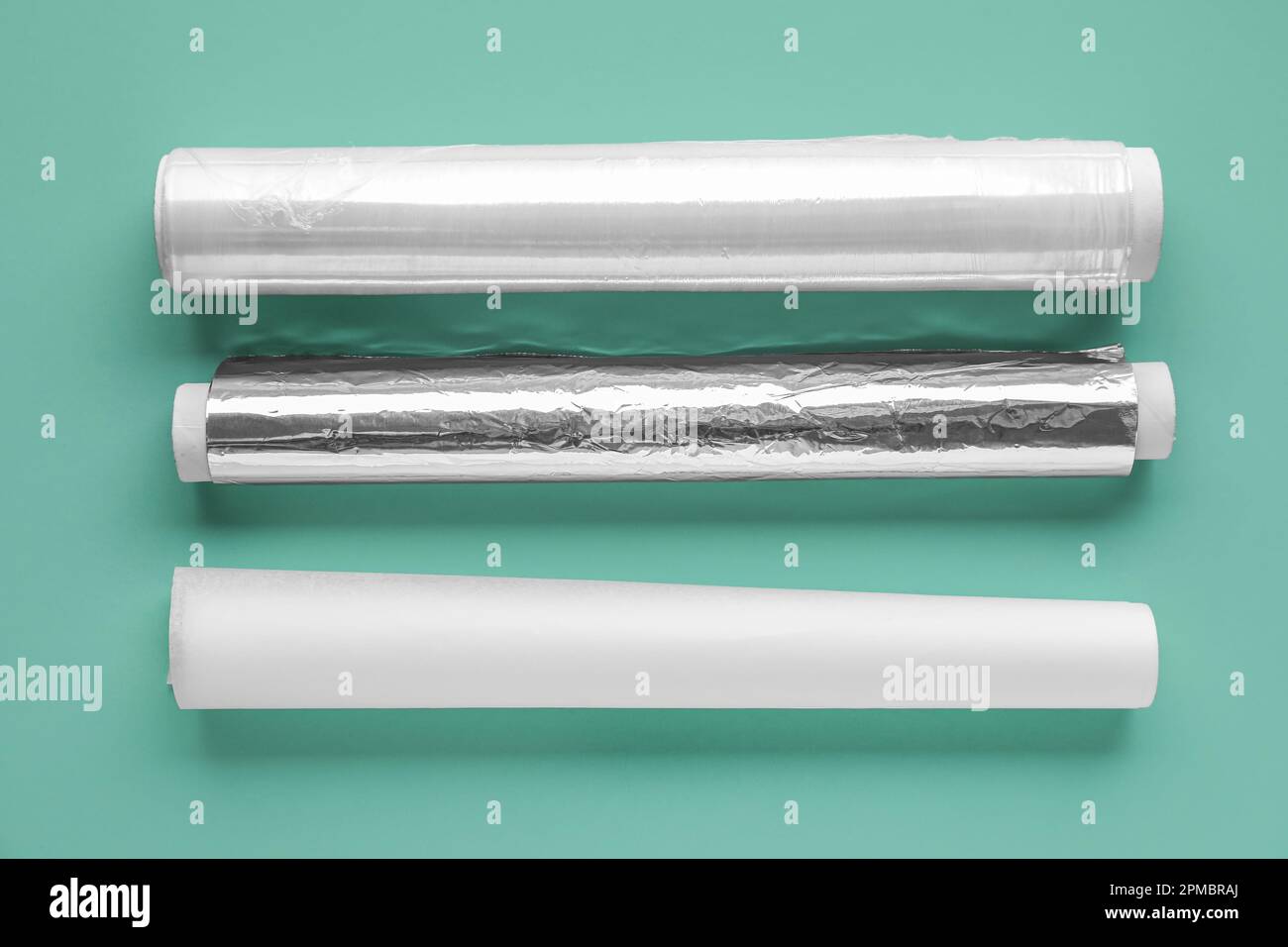 Rolls of baking paper, aluminium foil and food film on color background ...