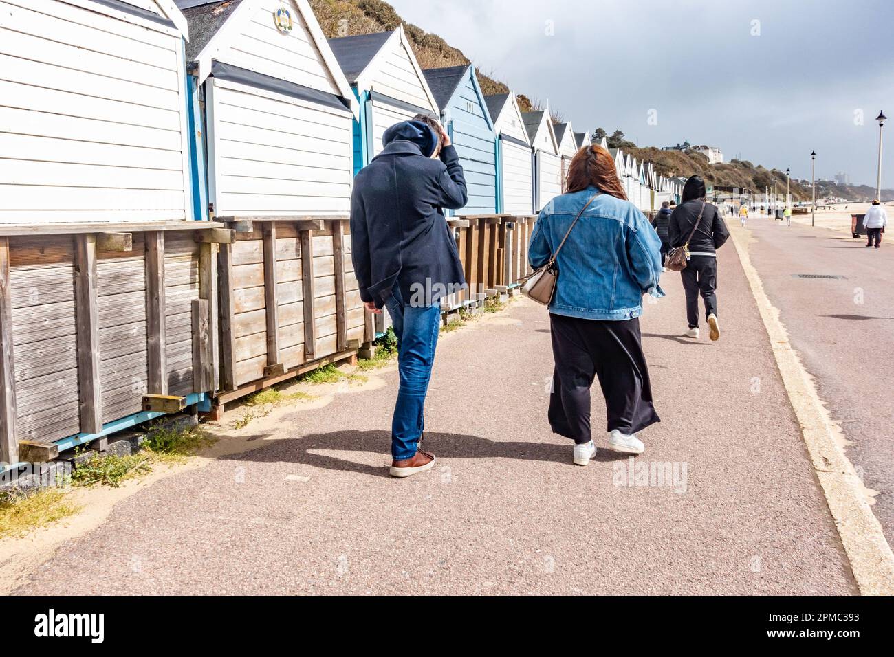 People walk along a path in front of beach huts on Bournemouth Beach in ...