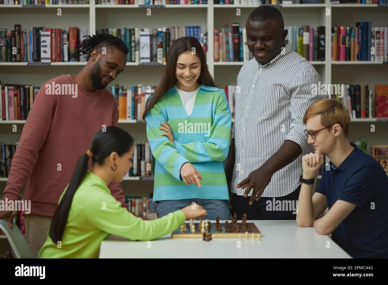 Side view at two young people playing chess with diverse group of ...
