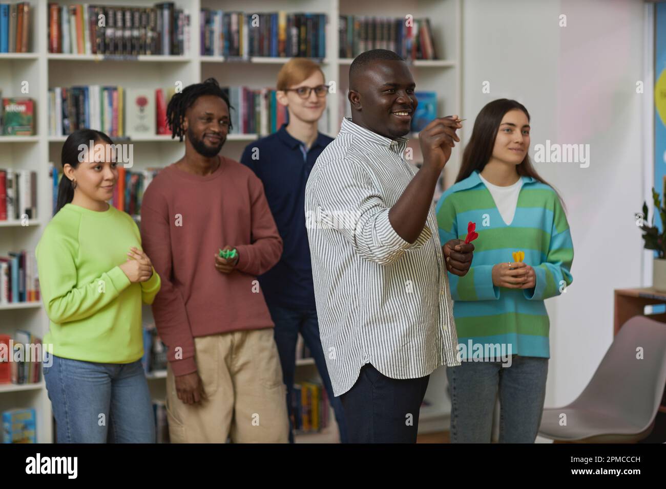 Diverse group of young people playing darts game indoors and having fun ...