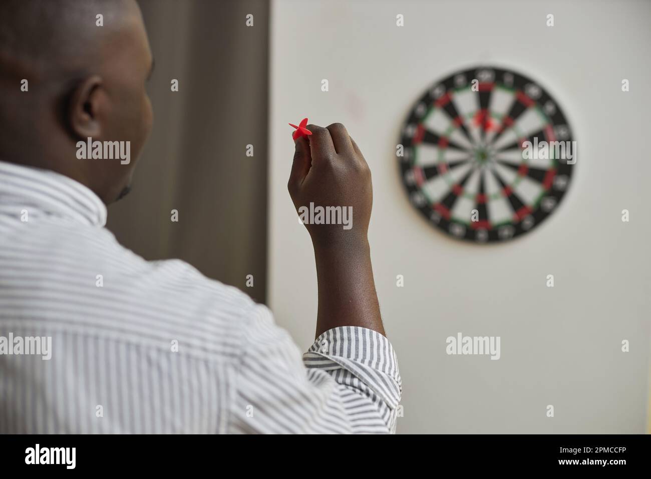 Minimal back view of African American man playing darts and aiming shot ...