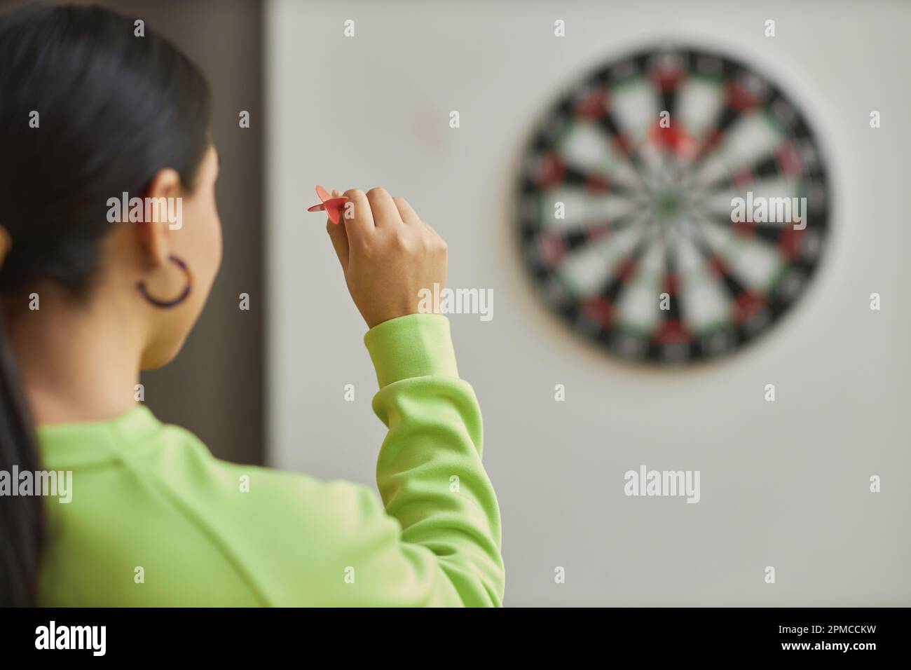 Back view closeup of young woman playing darts and aiming shot, copy ...