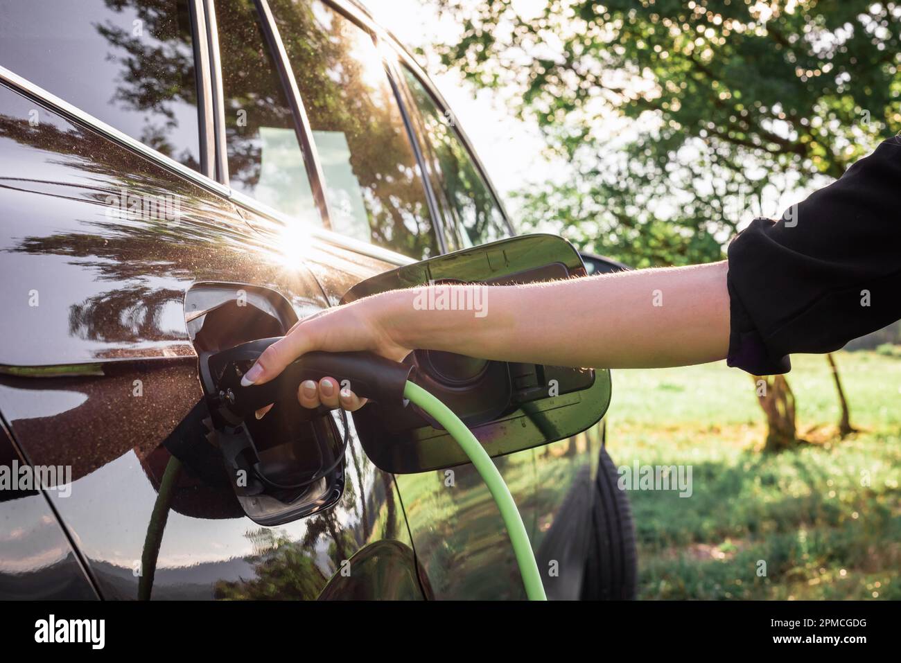 Female hand putting a cable charger in an electric car illuminated by ...