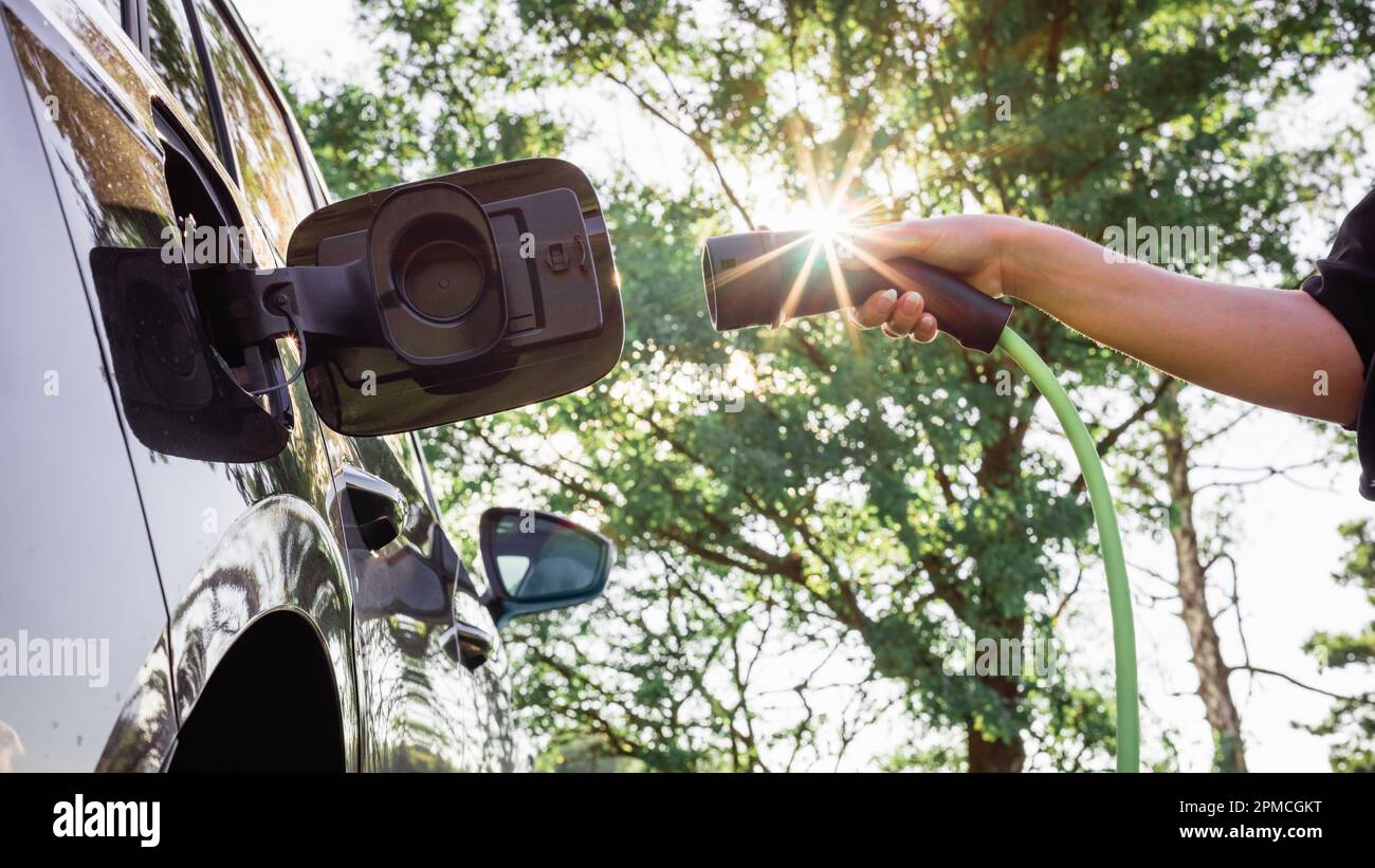 Female hand putting a cable charger in an electric car illuminated by ...