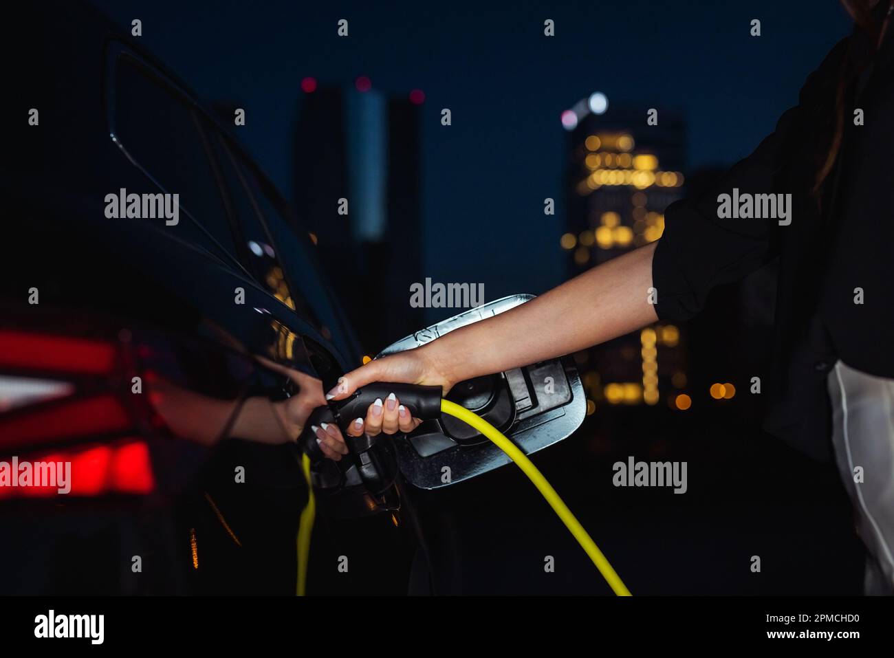 Female hands opening an electric car charging socket cap and plugging ...