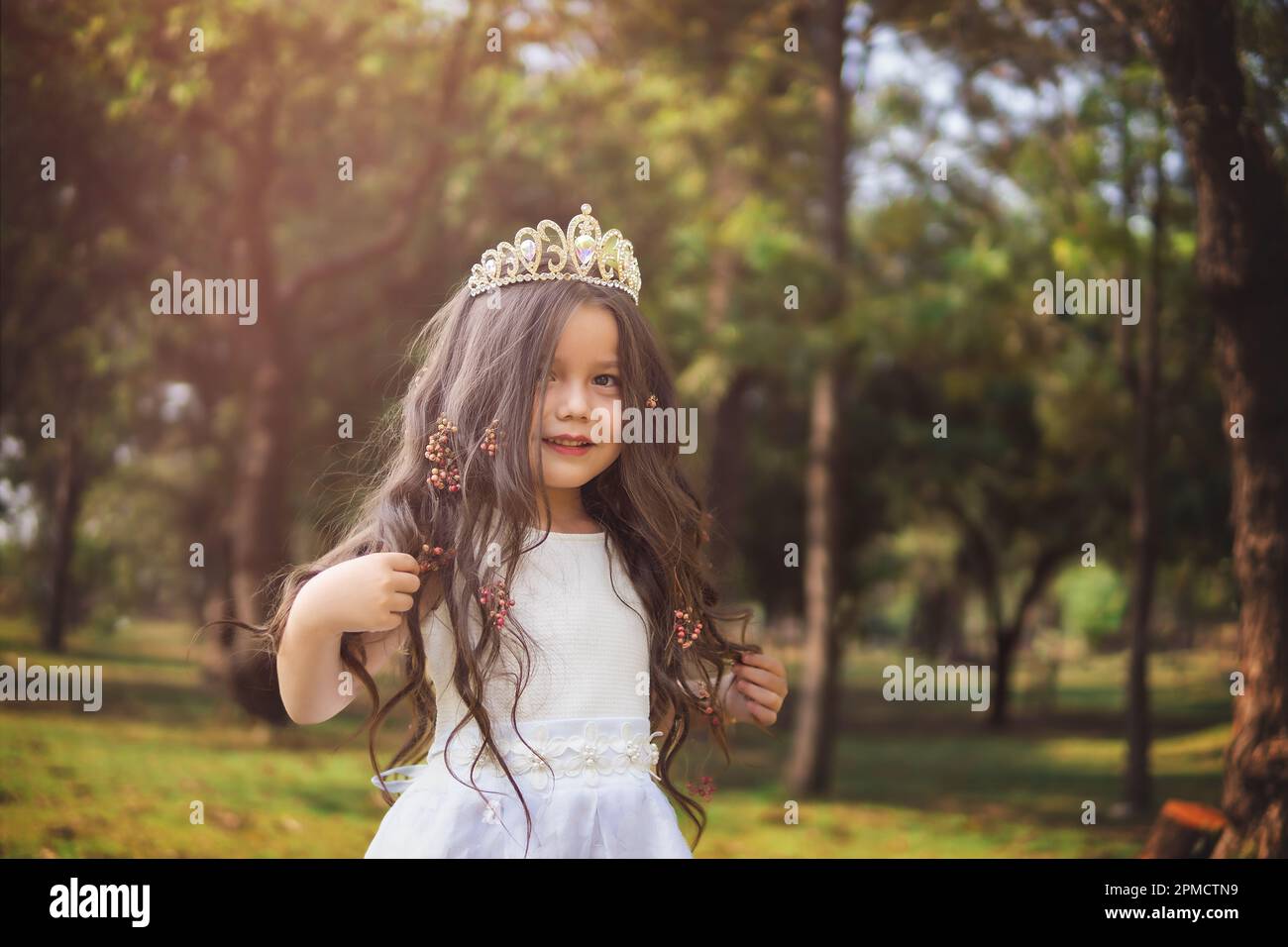 Little girl in white dress and princess crown, she plays with her long ...