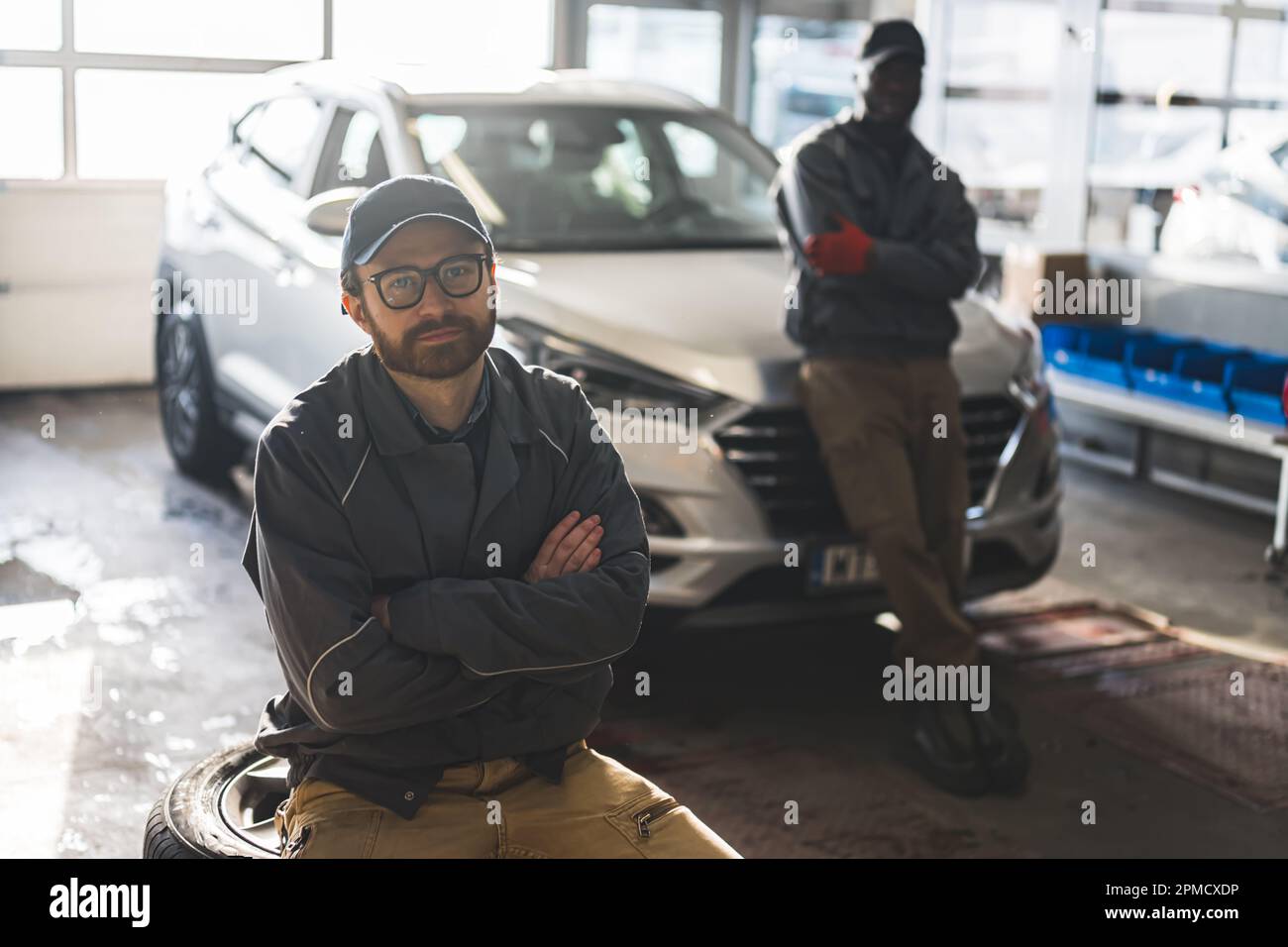 medium shot of a Caucasian auto mechanic sitting on wheels and an ...