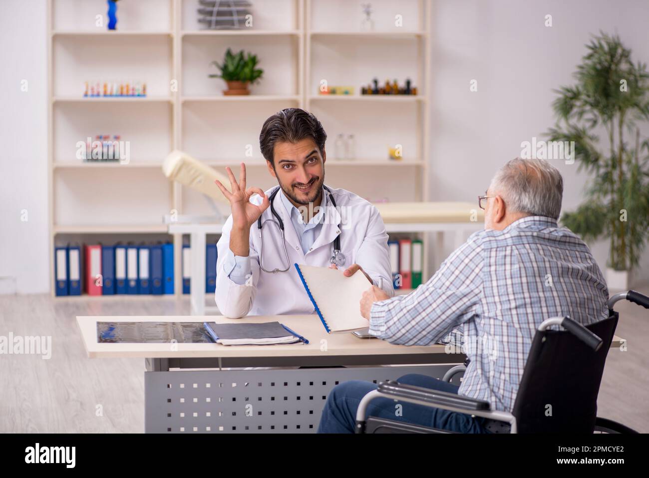 Old male patient in wheelchair visiting young male doctor Stock Photo ...