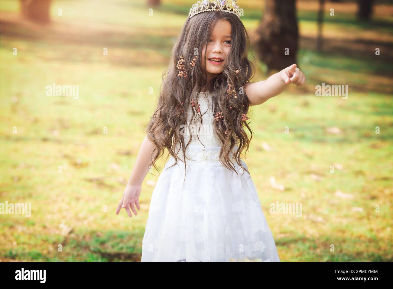 Little girl in white dress and princess crown, she poses for the camera ...