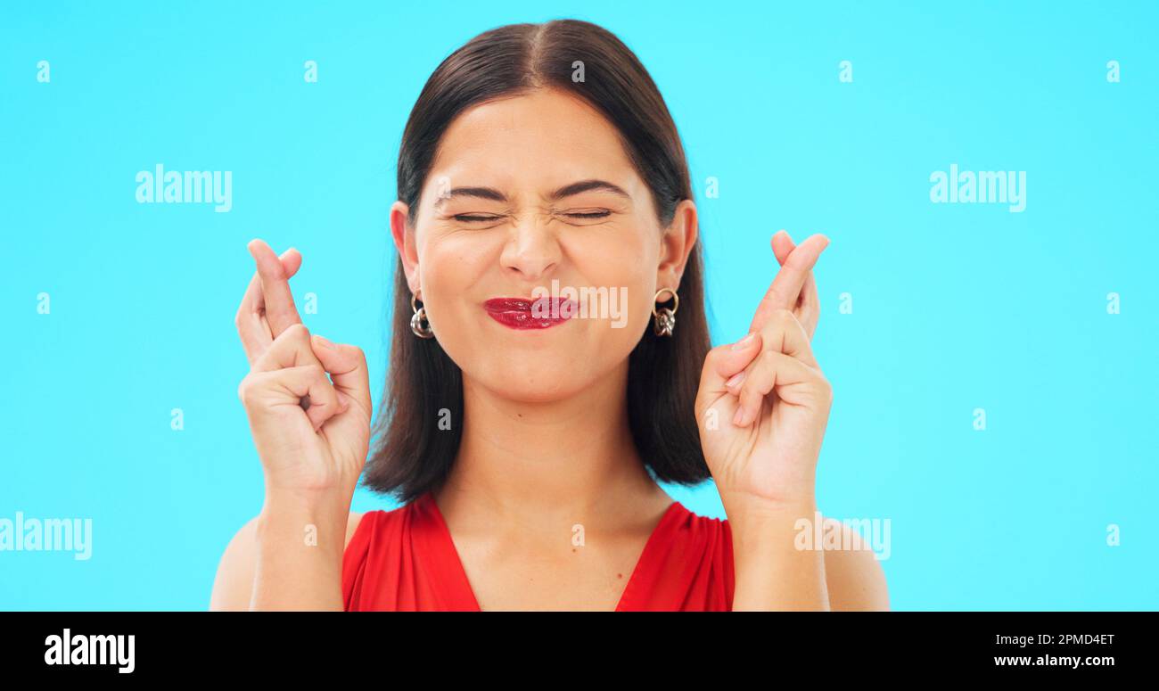 Happy, woman and face with fingers crossed on blue background, studio ...