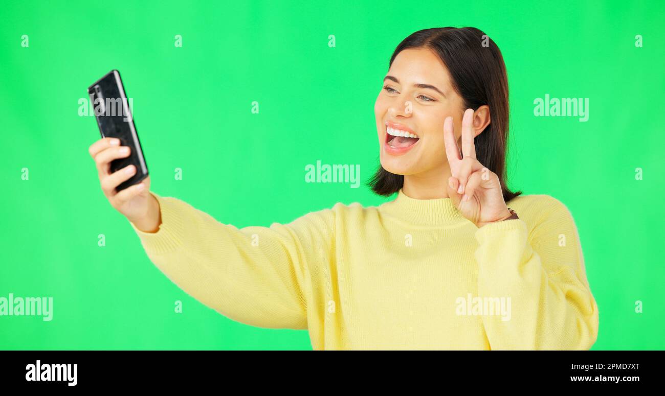 Happy woman, face and selfie on green screen with peace sign and facial expressions against ...