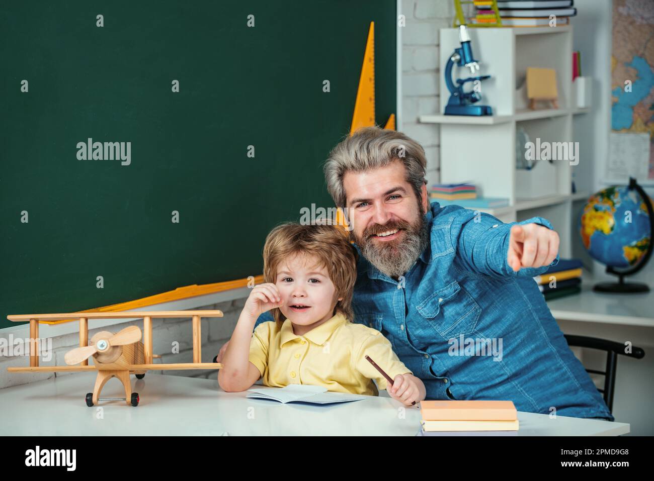 Cute child boy with teacher in classroom near blackboard desk. Tutoring ...